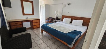 Quarto de hotel com cama, escrivaninha, cadeira, televisão e guarda-roupa.