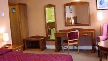 Quarto de hotel com cama, escrivaninha, cadeira, espelho e mesa de cabeceira.