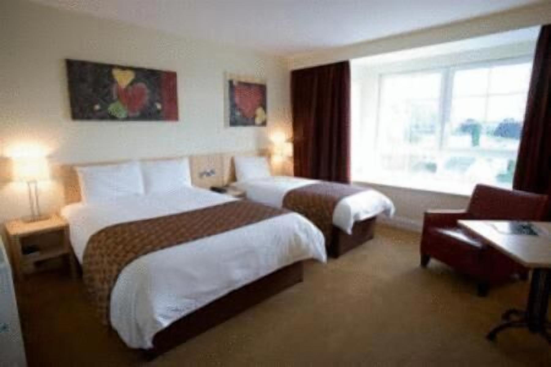 Quarto de hotel com duas camas, uma escrivaninha e uma janela.
