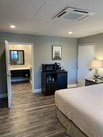 Quarto de hotel com cama, escrivaninha com computador, micro-ondas e armário pequeno.