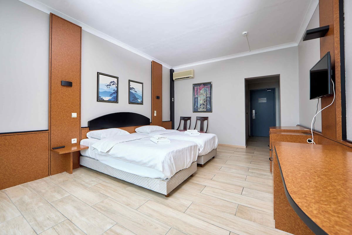 Quarto de hotel com duas camas, uma escrivaninha de madeira, televisão de tela plana e obras de arte nas paredes.