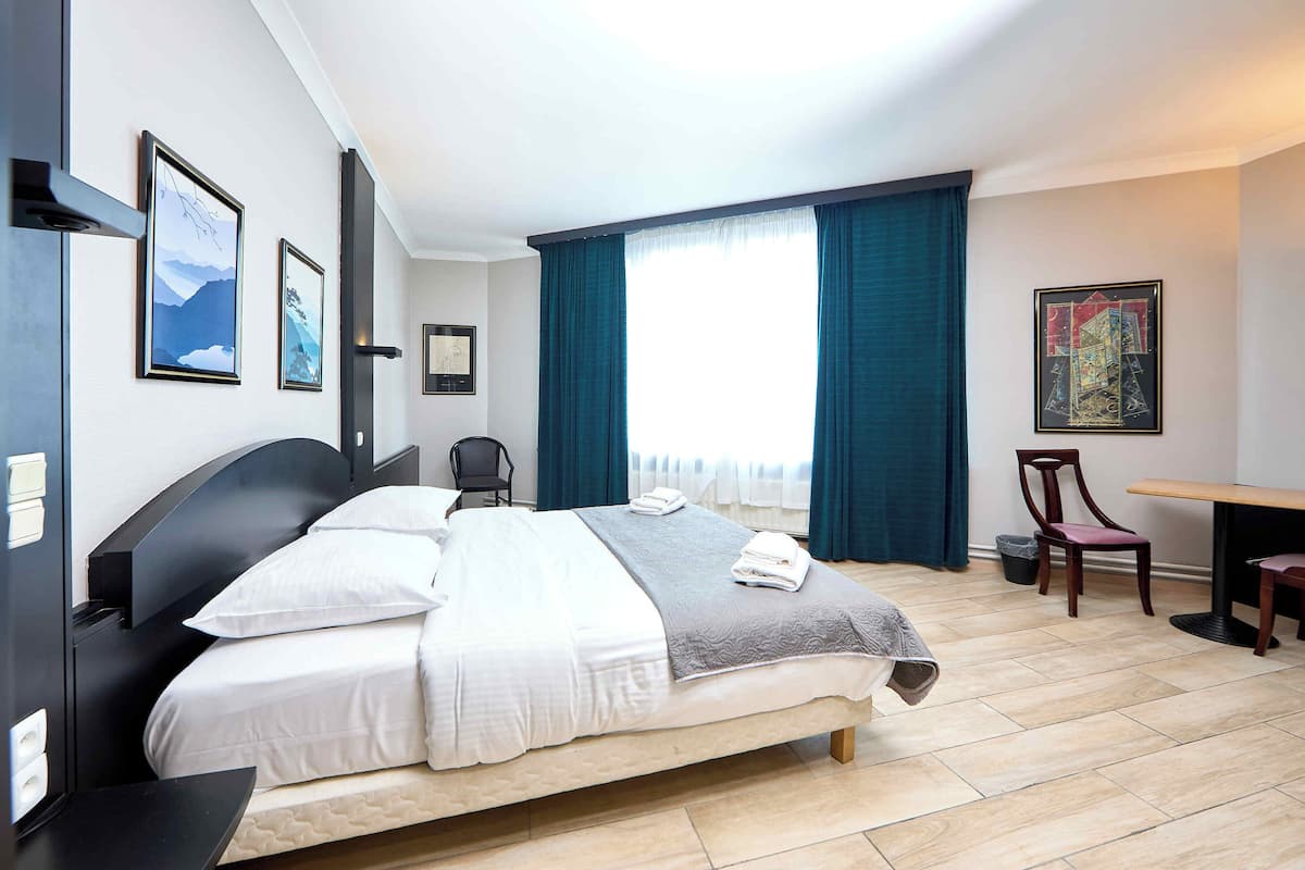 Quarto de hotel com cama, escrivaninha, cadeira e obras de arte nas paredes.