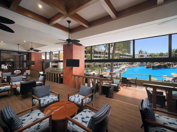 Ampla área de estar ao ar livre com diversas opções de assento, vista para a piscina e um bar.