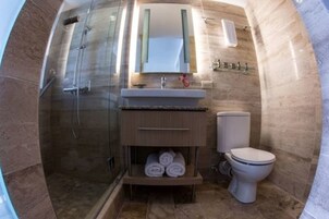 Uma casa de banho moderna com chuveiro em cabine de vidro, lavatório com espelho e sanita.