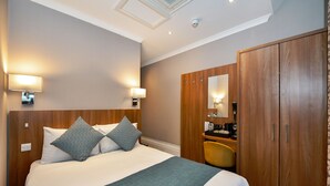 Quarto de hotel com cama grande, guarda-roupa de madeira e escrivaninha com cadeira.