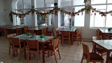 Uma área de refeições com mesas e cadeiras de madeira, decorada com guirlandas de Natal.