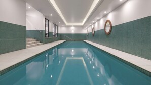 Piscina com borda azulejada, escadaria que leva a uma porta e teto com iluminação embutida.