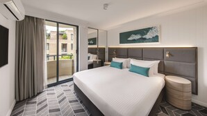 Quarto de hotel moderno com uma cama grande, mesa de cabeceira pequena, espelho e vista para a varanda.