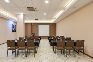 Uma sala de conferência com fileiras de cadeiras, uma tela de projetor e uma lousa.