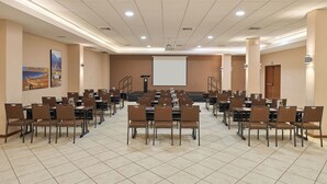 Uma sala de conferências com várias mesas e cadeiras, uma tela de projetor e um amplo janela.