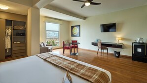 Quarto de hotel com cama, escrivaninha, cadeira, televisão e vista da cidade.