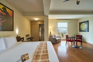 Quarto de hotel com cama, escrivaninha, cadeira, sofá, janela e um quadro na parede.