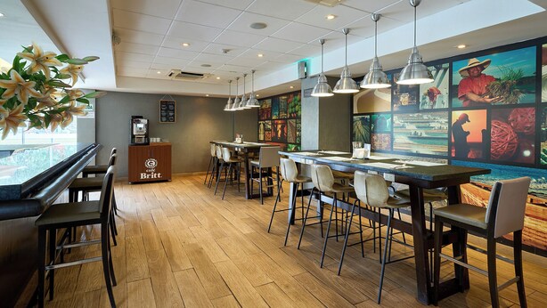 Interior de café com piso de madeira, bancada, luminárias pendentes e parede com obras de arte coloridas.