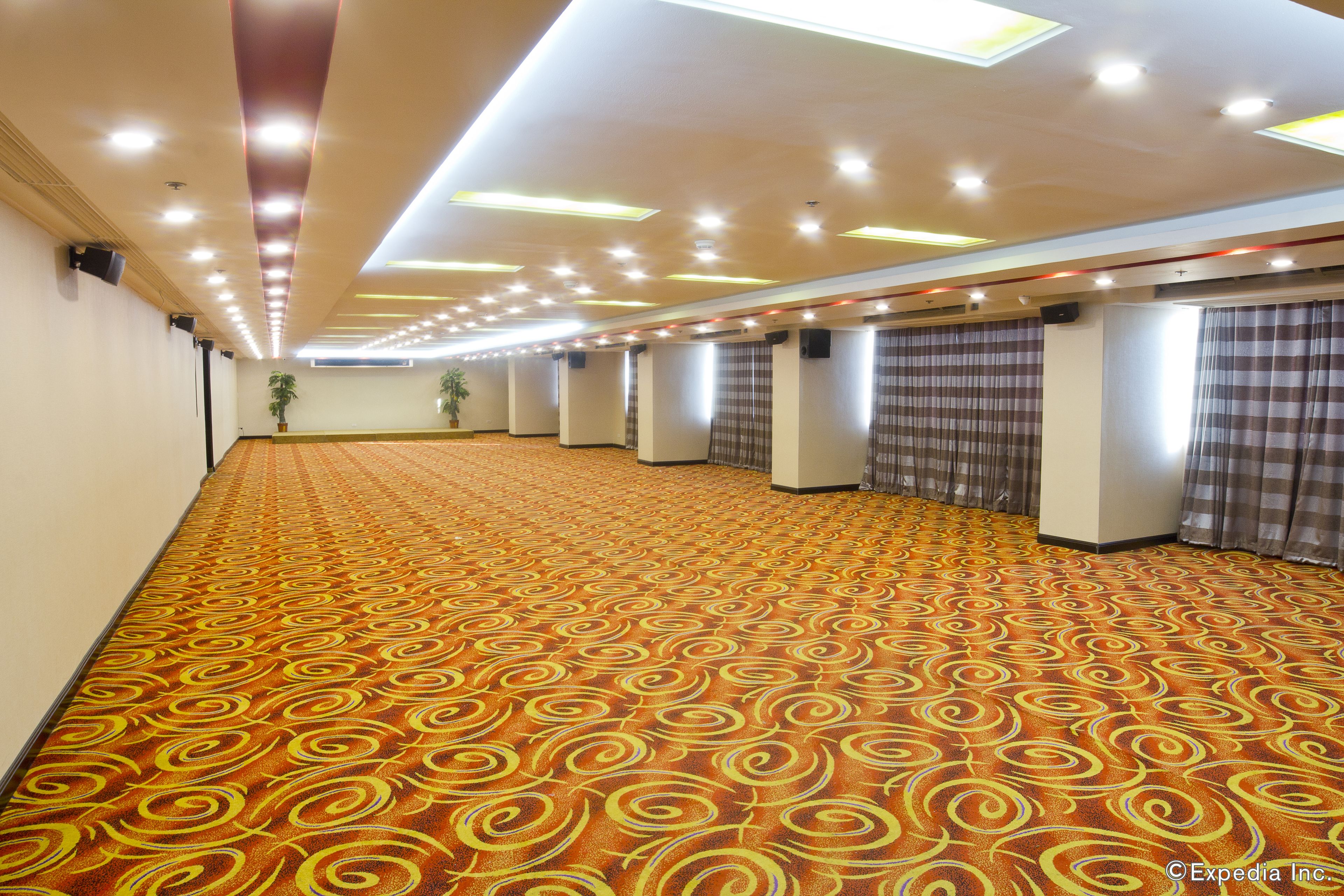 Um salão amplo com carpete, piso estampado, iluminação embutida e cortinas nas janelas.