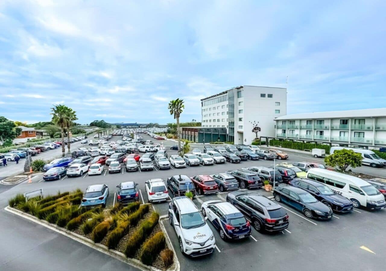 Um estacionamento com vários carros, um edifício de design moderno e um céu claro.