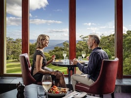 Duas pessoas jantando à mesa com uma vista panorâmica de um campo de golfe e montanhas.