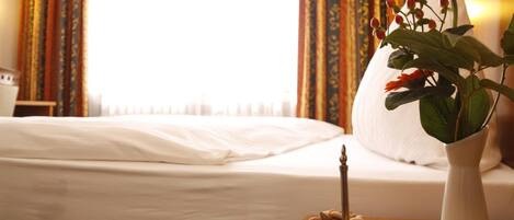Quarto de hotel com uma cama bem arrumada, um vaso com flores e uma tigela de lanches sobre uma mesa de madeira.