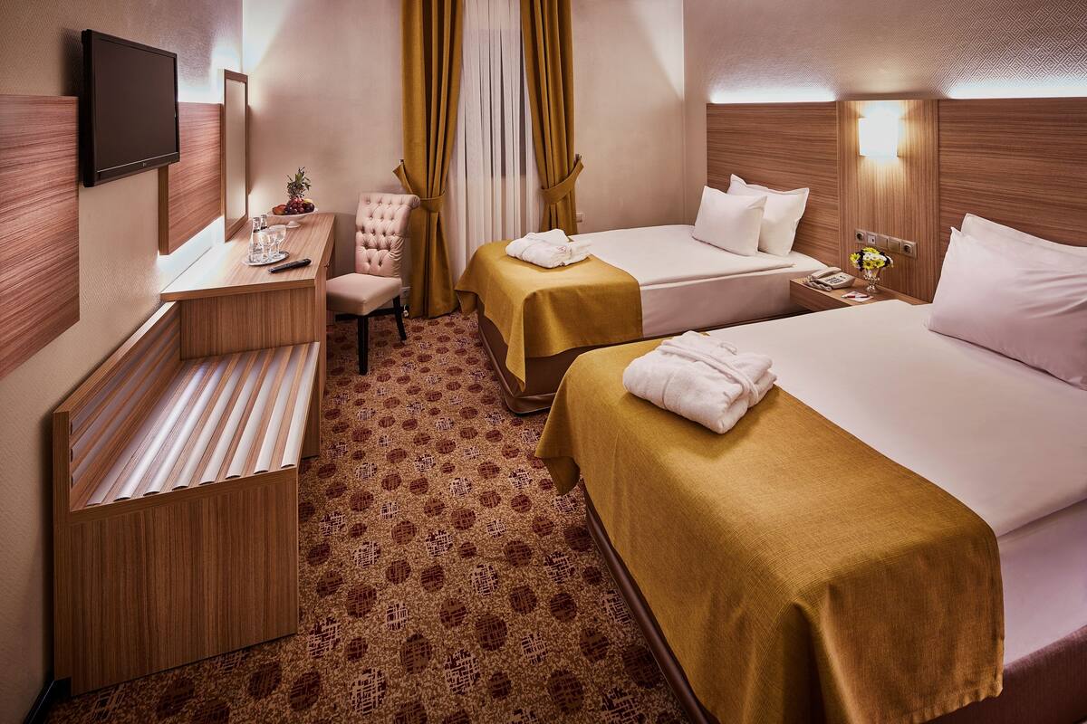 Quarto de hotel com duas camas, uma escrivaninha, uma cadeira e uma televisão.