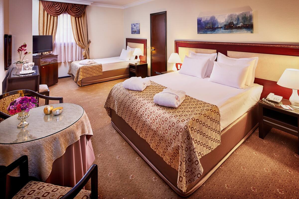 Quarto de hotel com duas camas, televisão, secretária com candeeiro e um quadro na parede.