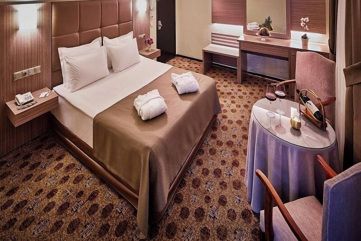Quarto de hotel com cama, mesa de cabeceira, escrivaninha com cadeira, mesa redonda com cadeira e espelho.