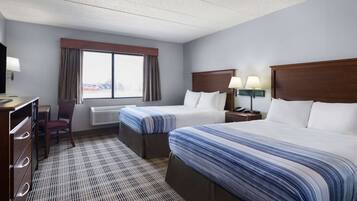 Quarto de hotel com duas camas, uma escrivaninha, uma cadeira e uma janela com cortinas.