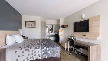 Quarto de hotel com cama, escrivaninha, cadeira, televisão e cozinha compacta.