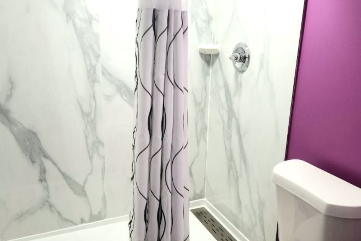 Casa de banho com cortina de chuveiro estampada com um padrão ondulado, sanita branca e parede de mármore.