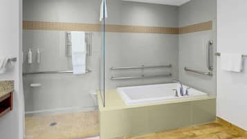 Uma casa de banho moderna com chuveiro, banheira e sanita. Existem barras de apoio para segurança, e um porta-toalhas é visível.
