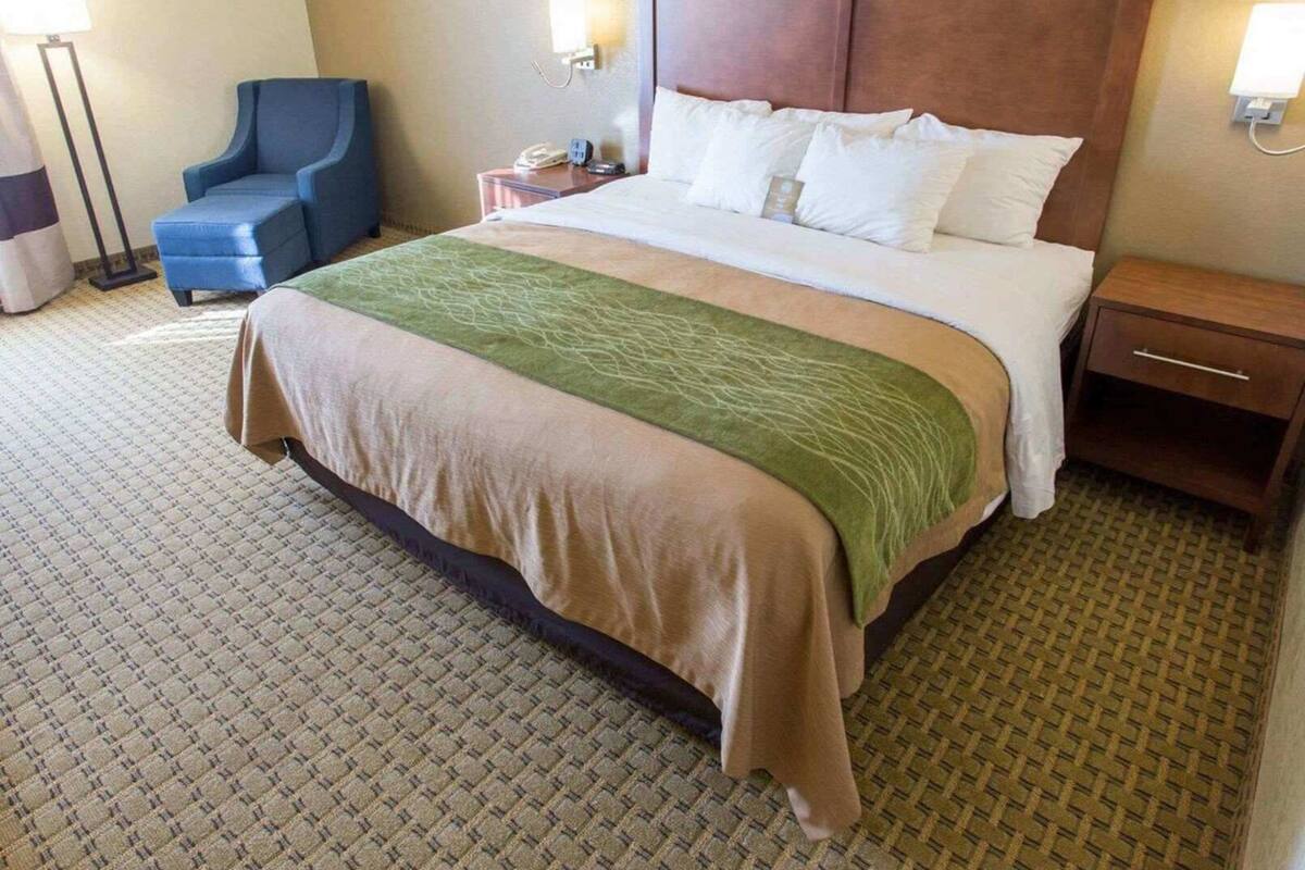 Quarto de hotel com cama, mesa de cabeceira, cadeira e luminária.