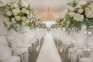 Um corredor de casamento com cadeiras brancas e arranjos florais em ambos os lados.