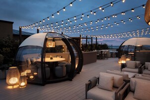 Terraço no telhado com luzes de corda, área de estar ao ar livre e espaço de jantar envidraçado.