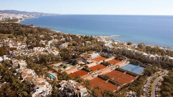 Vista aérea de uma cidade costeira com praia, campos de tênis e edifícios residenciais.
