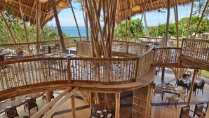 Estrutura de bambu em vários níveis, com áreas de refeições ao ar livre e vista para o oceano.