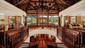 Um hall imponente com escadaria de madeira, grandes janelas e um lustre.