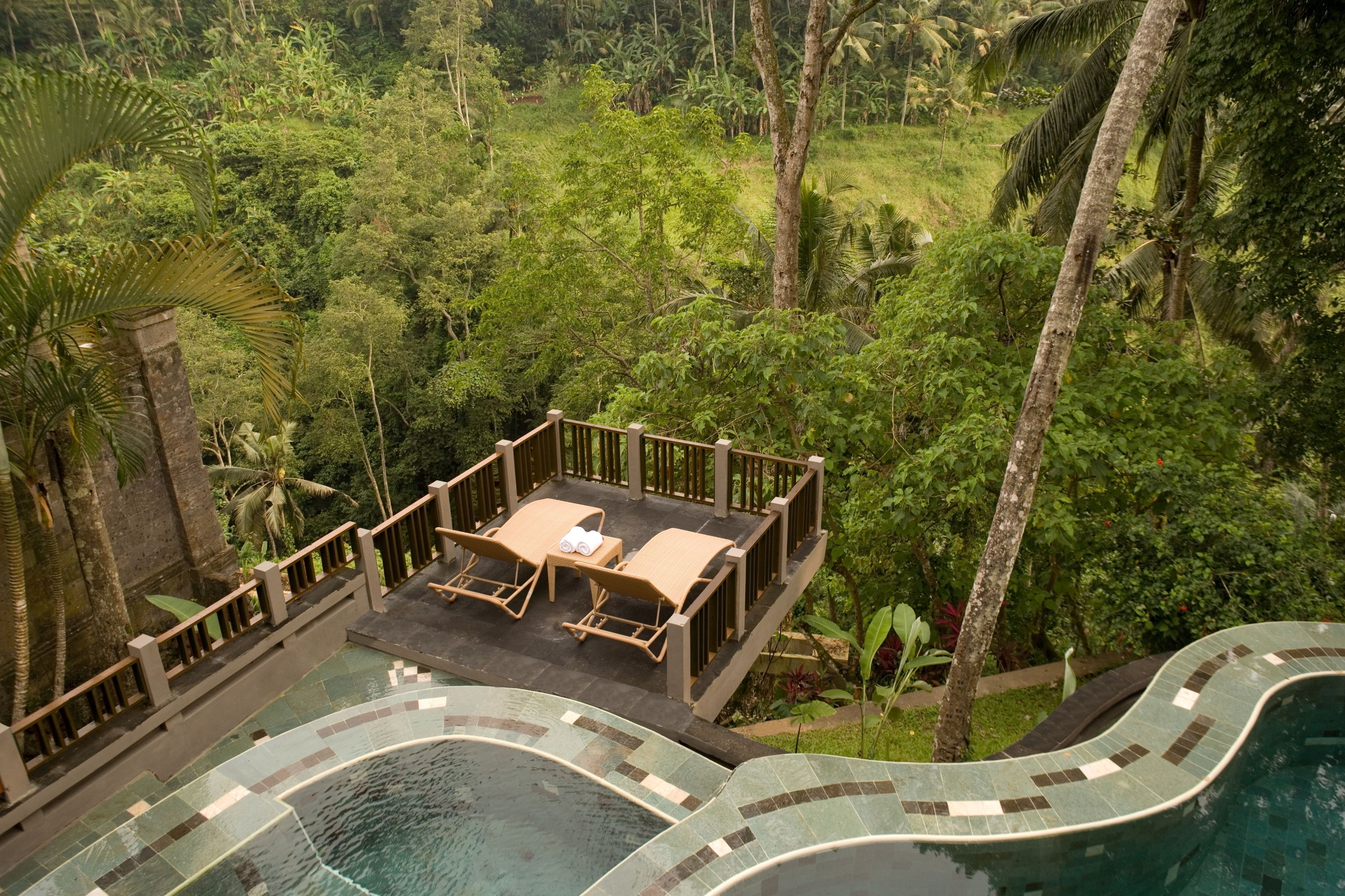Uma área de piscina com espreguiçadeira e uma mesa pequena, cercada por vegetação exuberante e palmeiras.