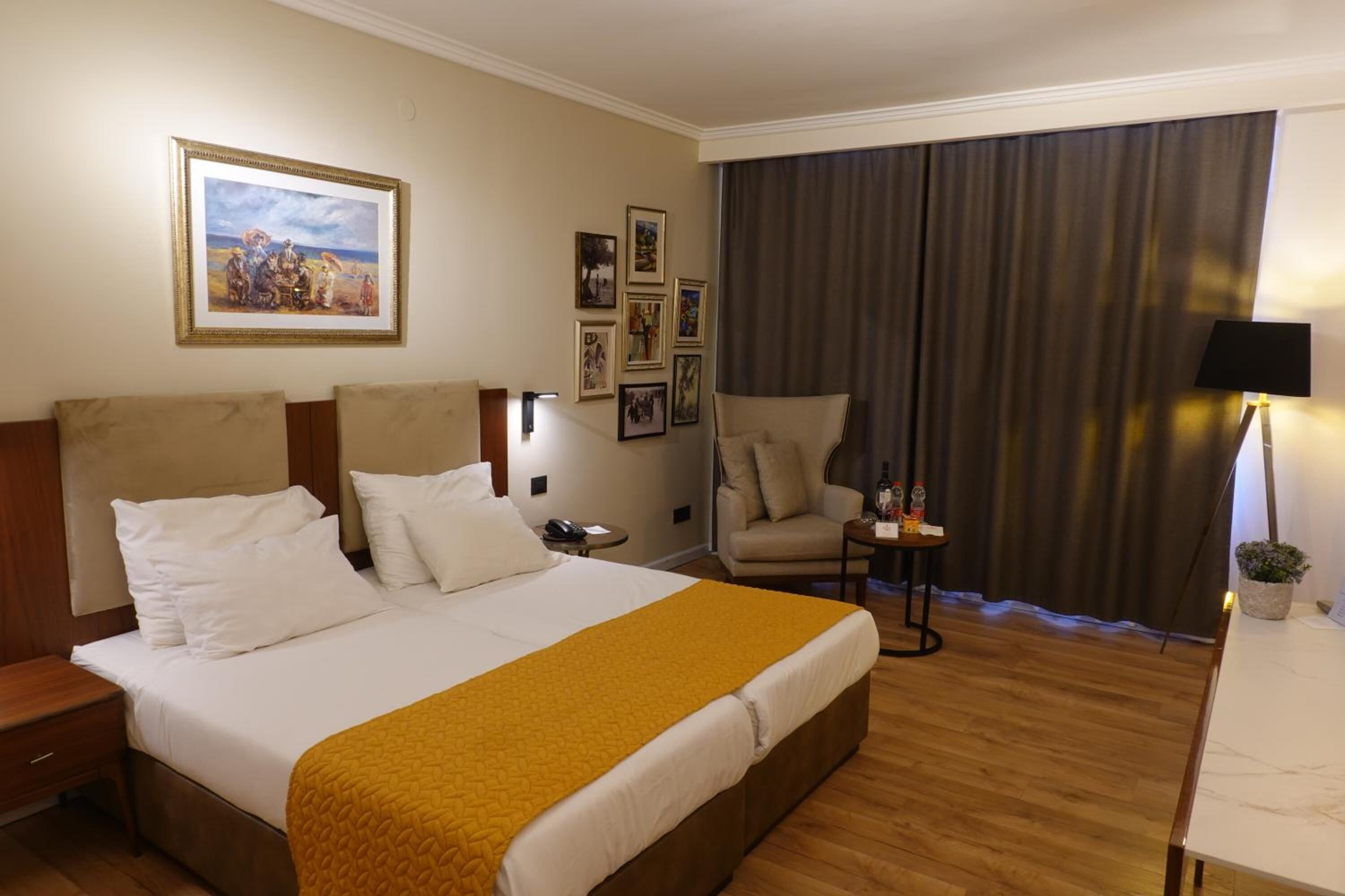 Quarto de hotel com uma cama grande, uma cadeira, uma mesa pequena com abajur e um quadro na parede.