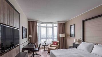 Quarto de hotel com uma cama grande, uma escrivaninha, uma cadeira, uma mesinha de centro com uma planta e uma televisão.
