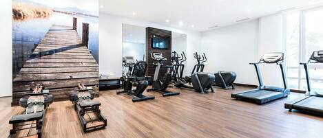Uma academia com equipamentos de ginástica, piso de madeira e uma janela grande.