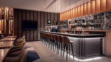 Uma área de bar moderna com um balcão comprido, banquetas e uma tela de televisão.