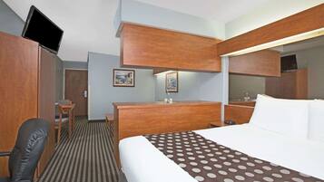 Quarto de hotel com cama, escrivaninha, cadeira, televisão e banheiro.