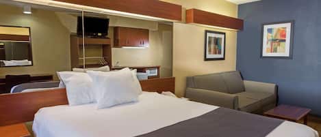 Quarto de hotel com cama grande, escrivaninha, cadeira, televisão e um quadro na parede.
