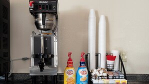 Máquina de café Bunn, um dispensador de café e variedade de cápsulas de café e garrafas de leite condensado em uma bancada.