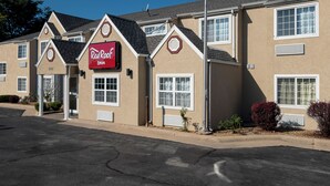 Um Red Roof Inn com design moderno, destacando uma placa proeminente em vermelho e branco, várias janelas e fachada bem conservada.
