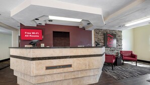 Uma área de recepção de hotel com balcão de mármore, parede vermelha e parede de pedra, e o letreiro da Red Roof Inn.