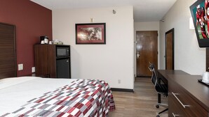 Quarto de hotel com cama, escrivaninha, televisão, micro-ondas e porta que dá para outro cômodo.