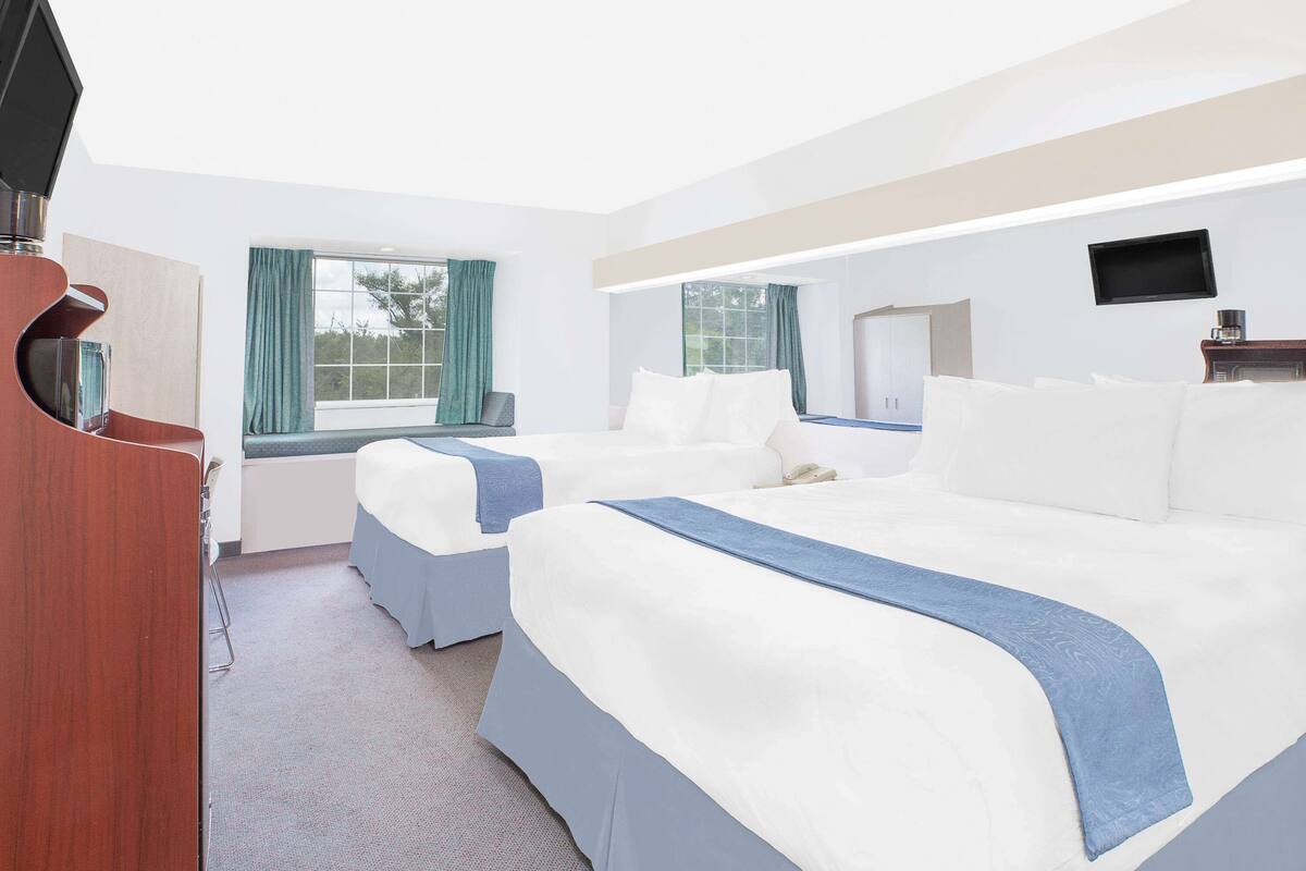 Quarto de hotel com duas camas, uma escrivaninha, uma televisão e uma janela com cortinas.