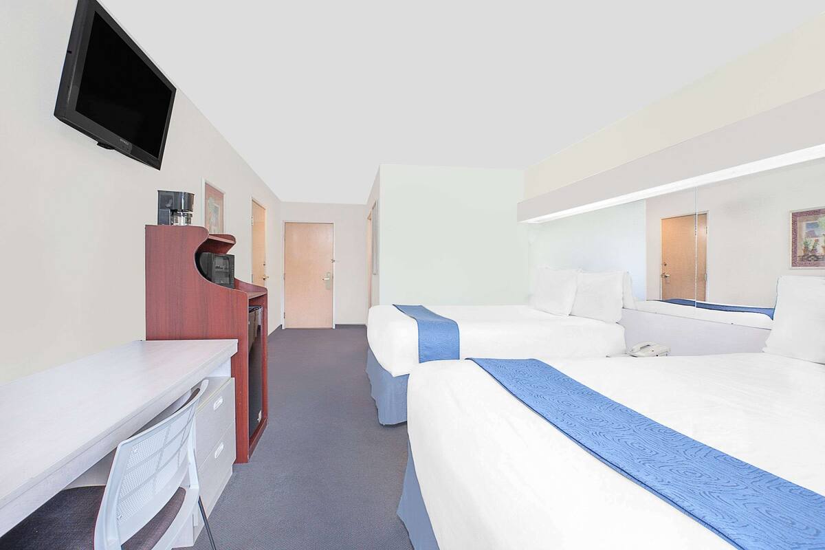 Quarto de hotel com duas camas, uma escrivaninha, uma cadeira, uma televisão e uma porta.