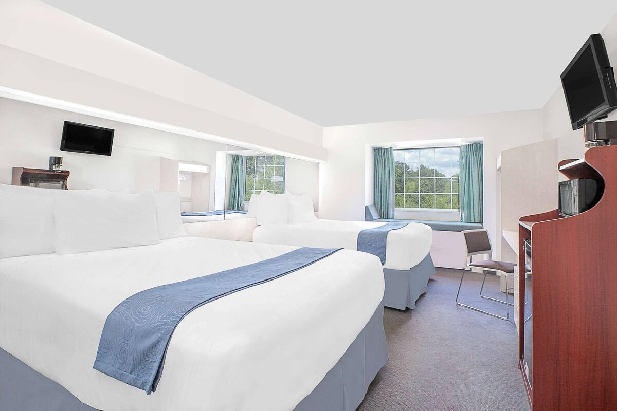 Quarto de hotel com duas camas, uma escrivaninha, televisão e janela com cortinas.