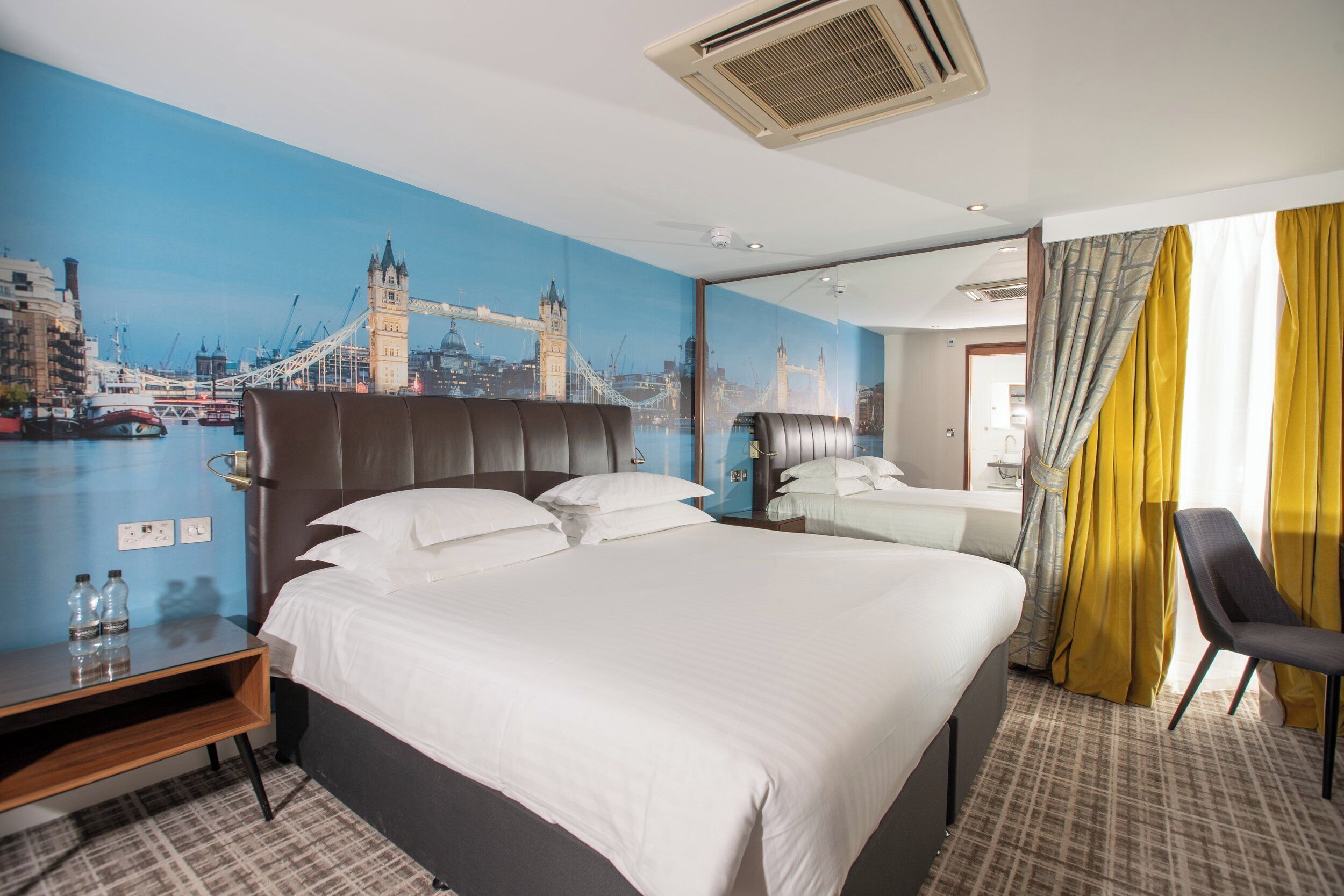 Quarto de hotel com uma cama grande, uma escrivaninha, uma cadeira e vista para um mural urbano.
