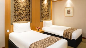 Quarto de hotel com duas camas, uma mesa de cabeceira com um vaso de flores e um quadro na parede.